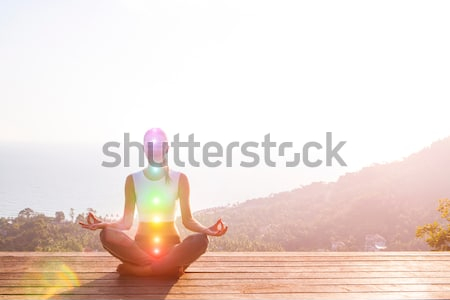 Постер на холсте Девушка в позе лотоса медитирует на свежем воздухе в лучах солнца с проекцией на туловище семи чакр 60см. x 40см.